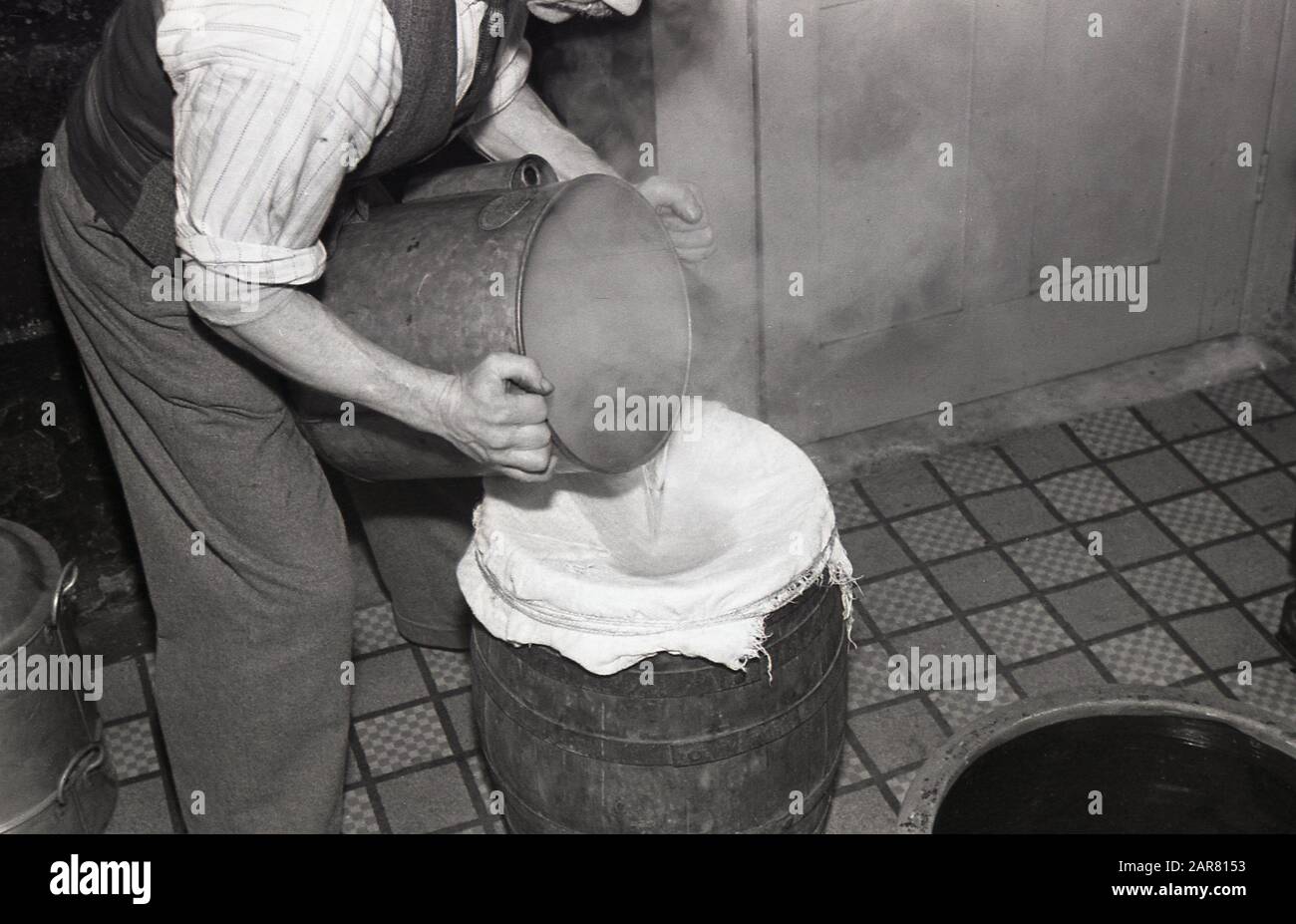 1950s, historical, making mead, a man pouring hot liquid from a metal ...