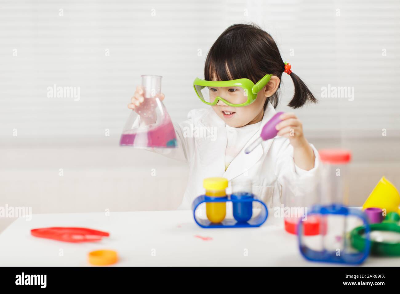 toddler girl pretend play scientist role at home against white ...