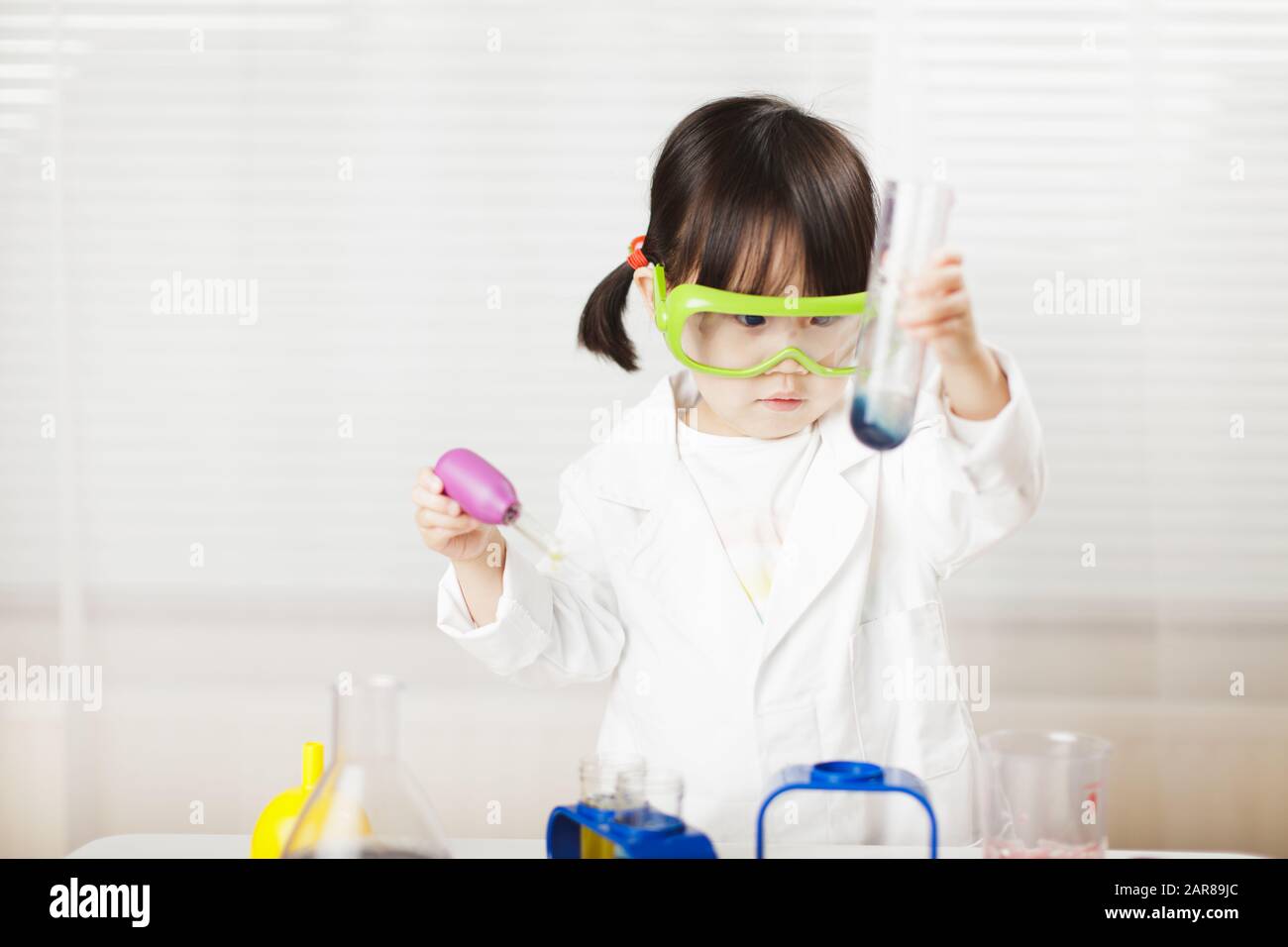 toddler girl pretend play scientist role at home against white ...