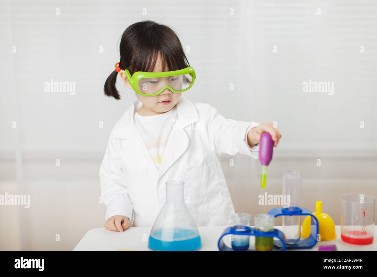 toddler girl pretend play scientist role at home against white ...