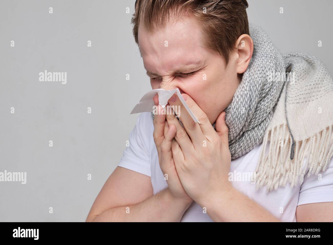A young man in a scarf holds it's being blown handkerchief for snot and ...