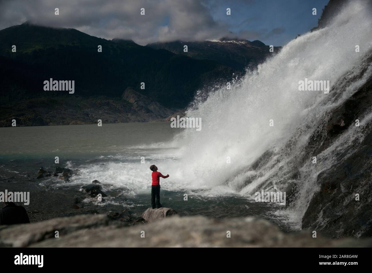 Lone tourist approaches the spray of the impressive waterfall on a ...