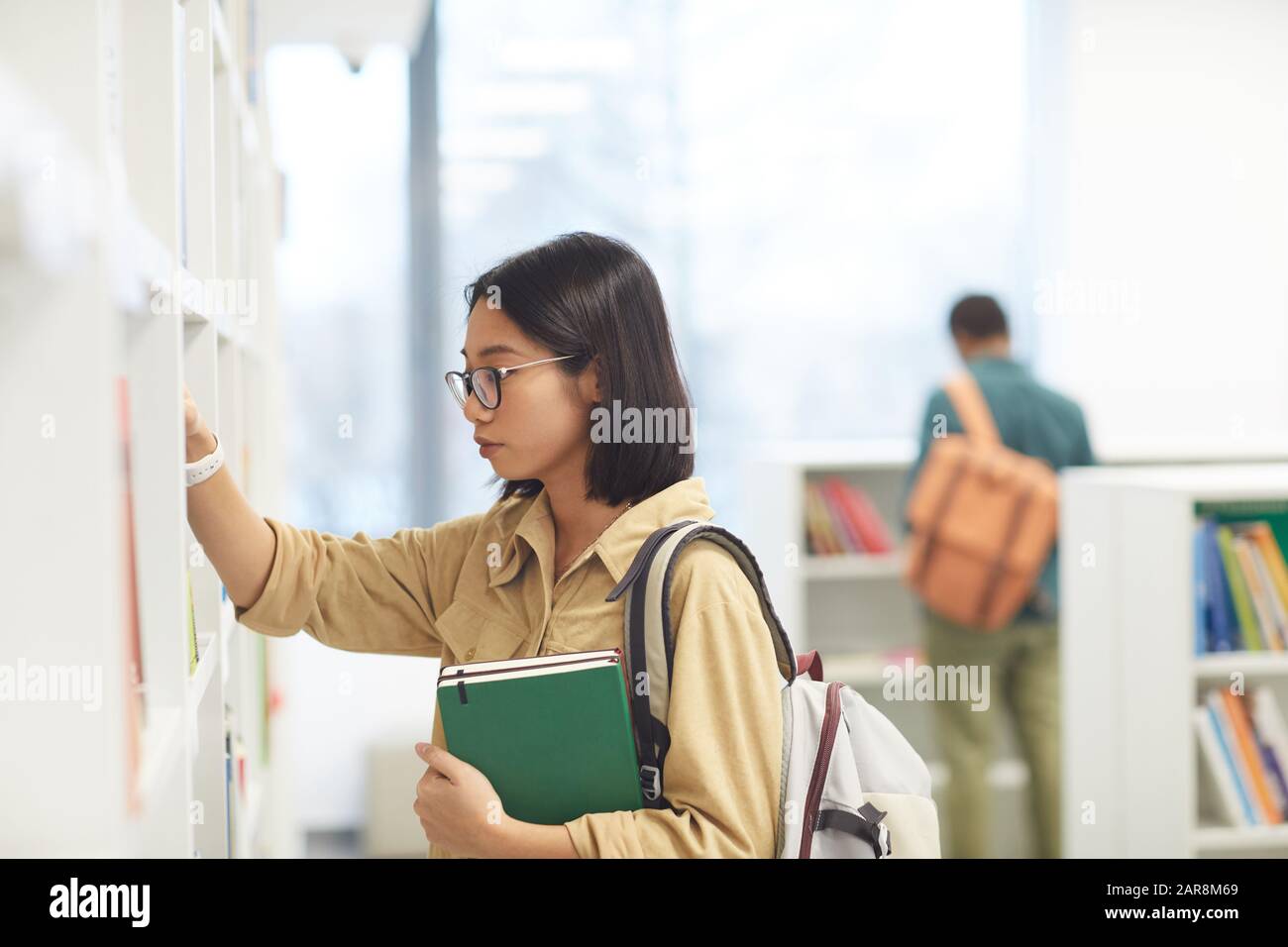 Side view portrait of female Asian student wearing glasses choosing ...