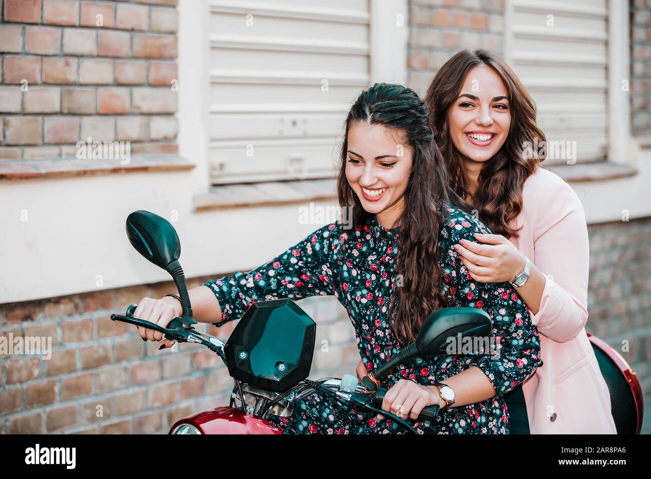 Having great fun together. Two happy female friends riding on motorbike ...