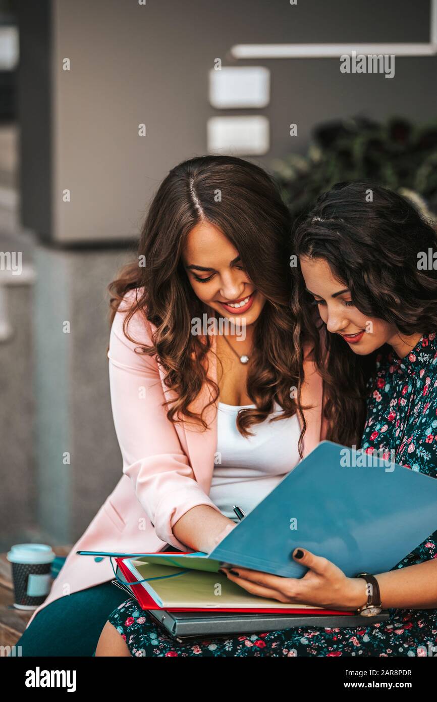 Two beautiful female friends, students checking paper notes and filling ...