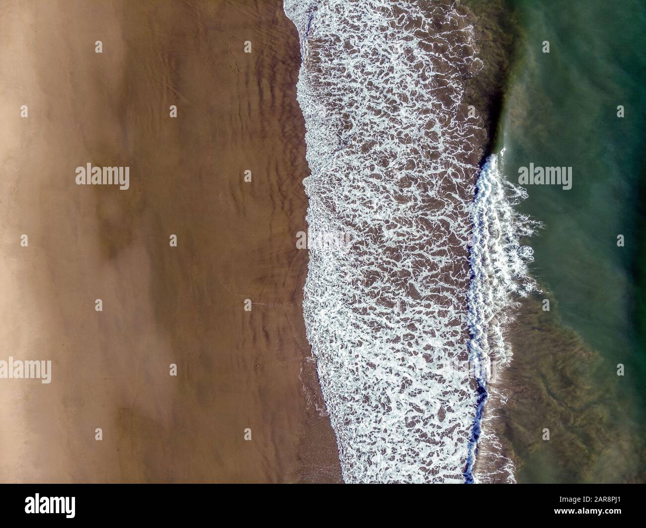 Looking down from above at waves washing up on sandy beach. Ocean water ...