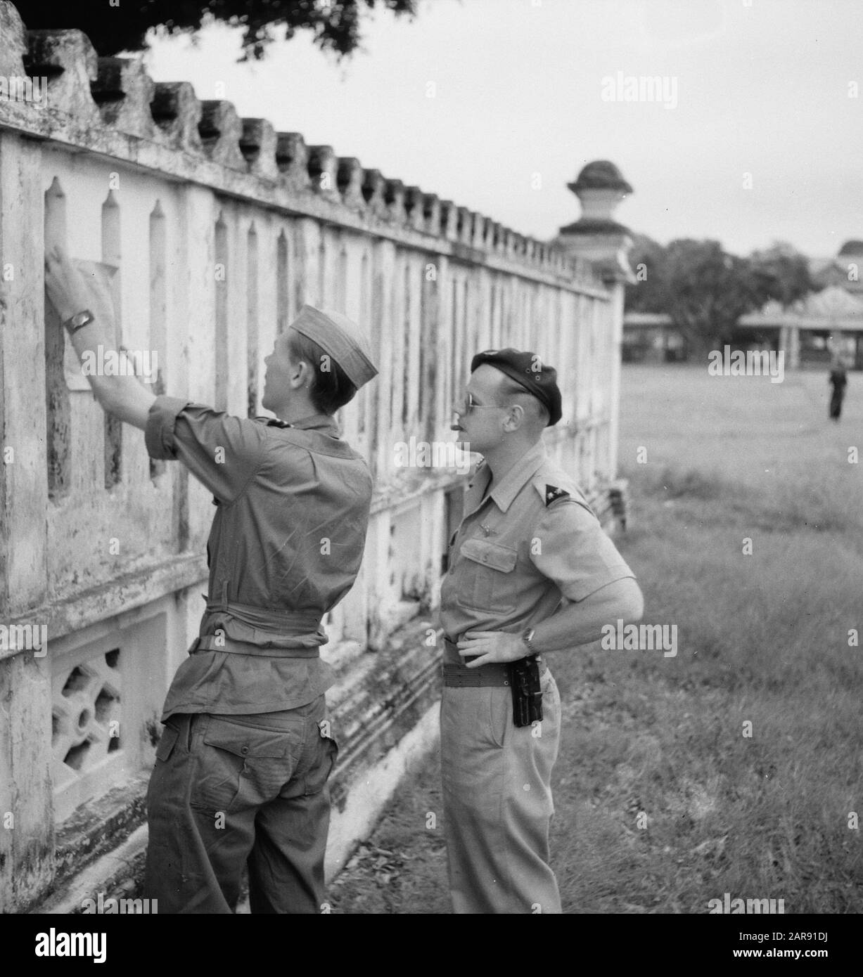 Two Dutch soldiers remove a communist pamphlet from a stone fence at ...