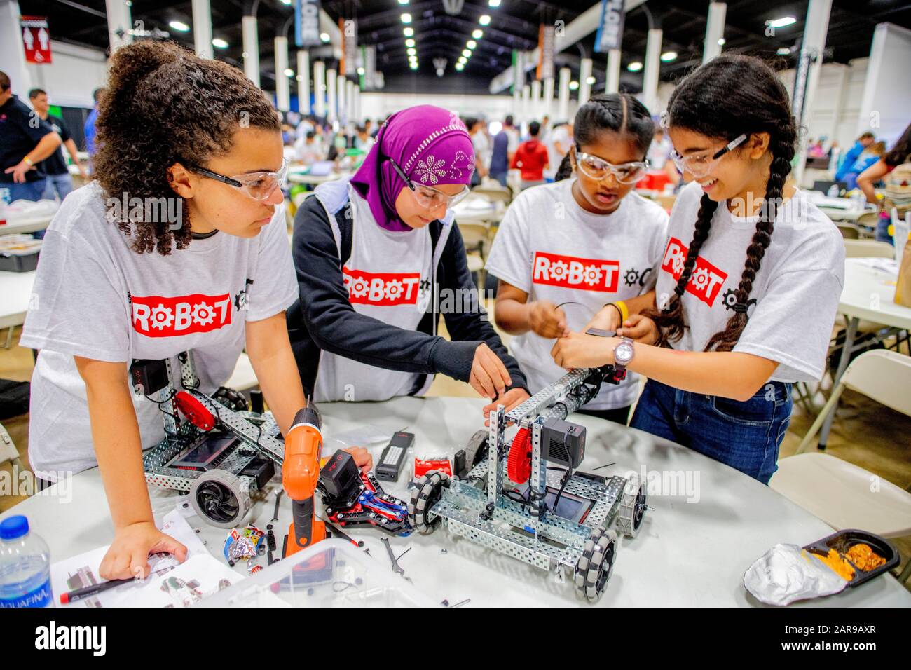 A multiracial high school girls' team assembles a robot at a high tech ...