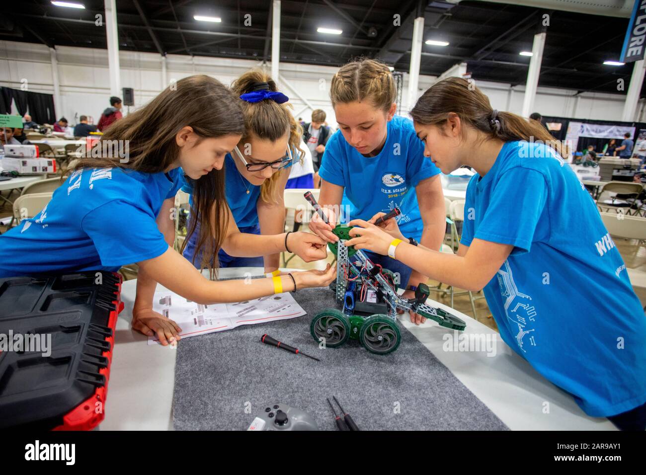A multiracial high school girls' team assembles a robot at a high tech ...