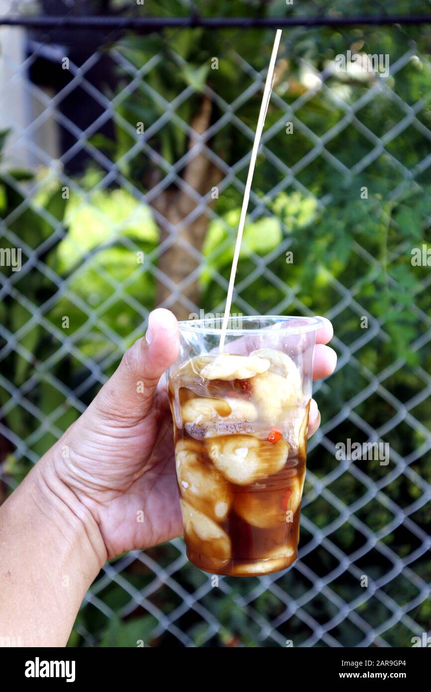 Photo of freshly cooked fish balls with sauce in a plastic cup held by ...