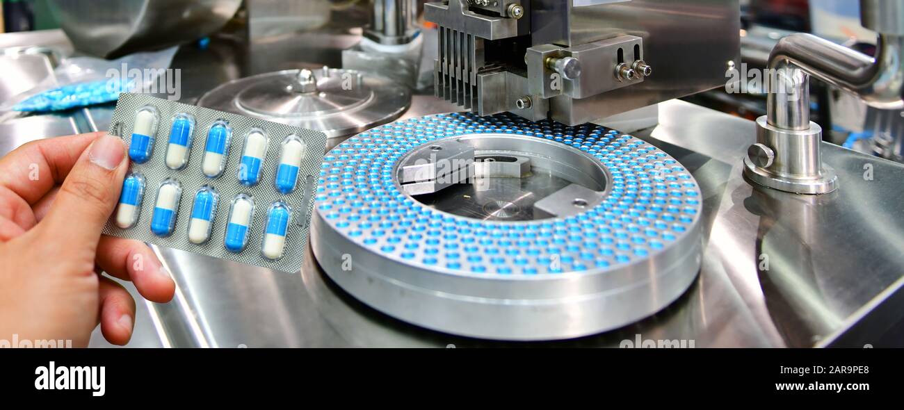 Hand holding blue capsule pack at medicine pill production line ...