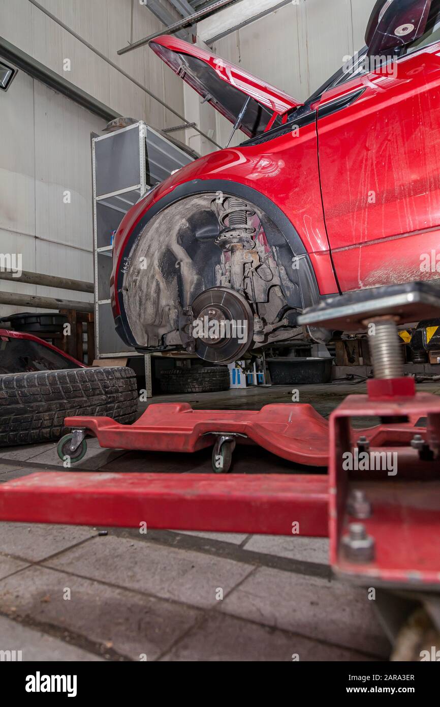 Red used car with an open hood raised on a lift for repairing the ...