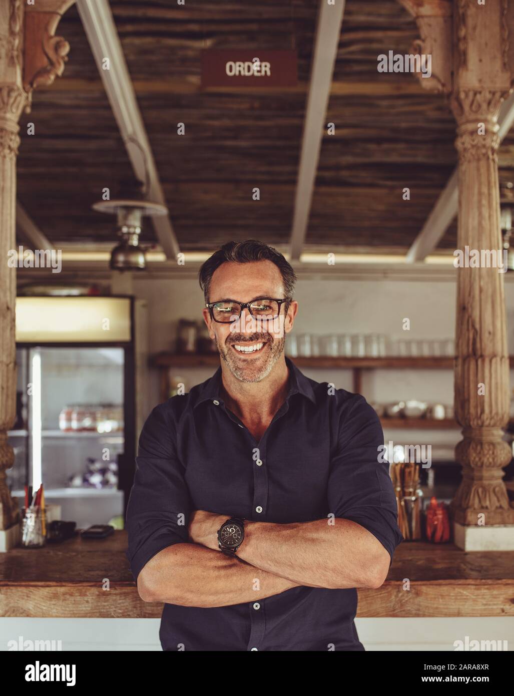 Portrait of a smiling cafe owner standing with his arms crossed ...