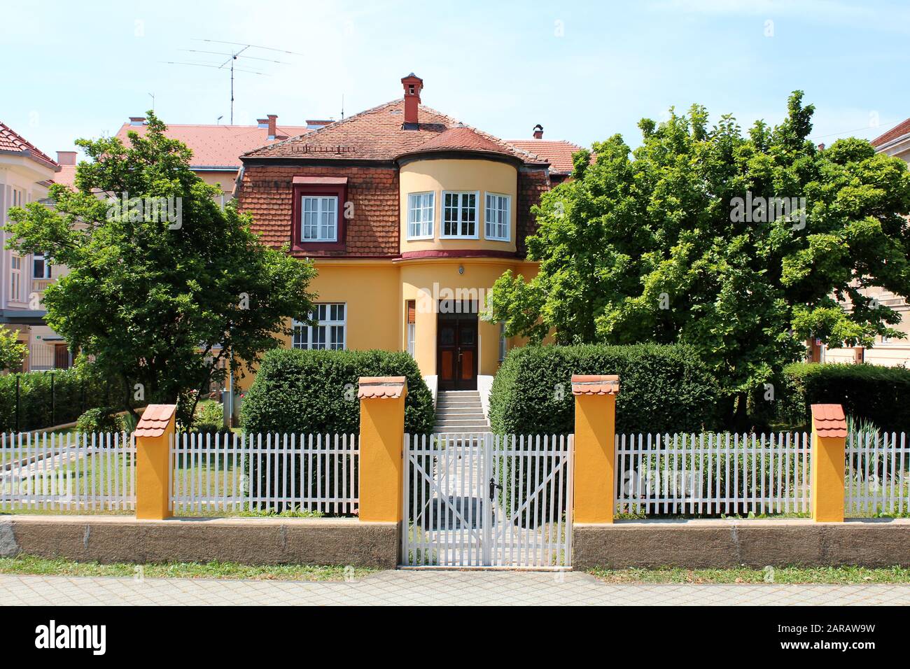 Renovated old suburban family house with new yellow facade surrounded with white picket fence ...