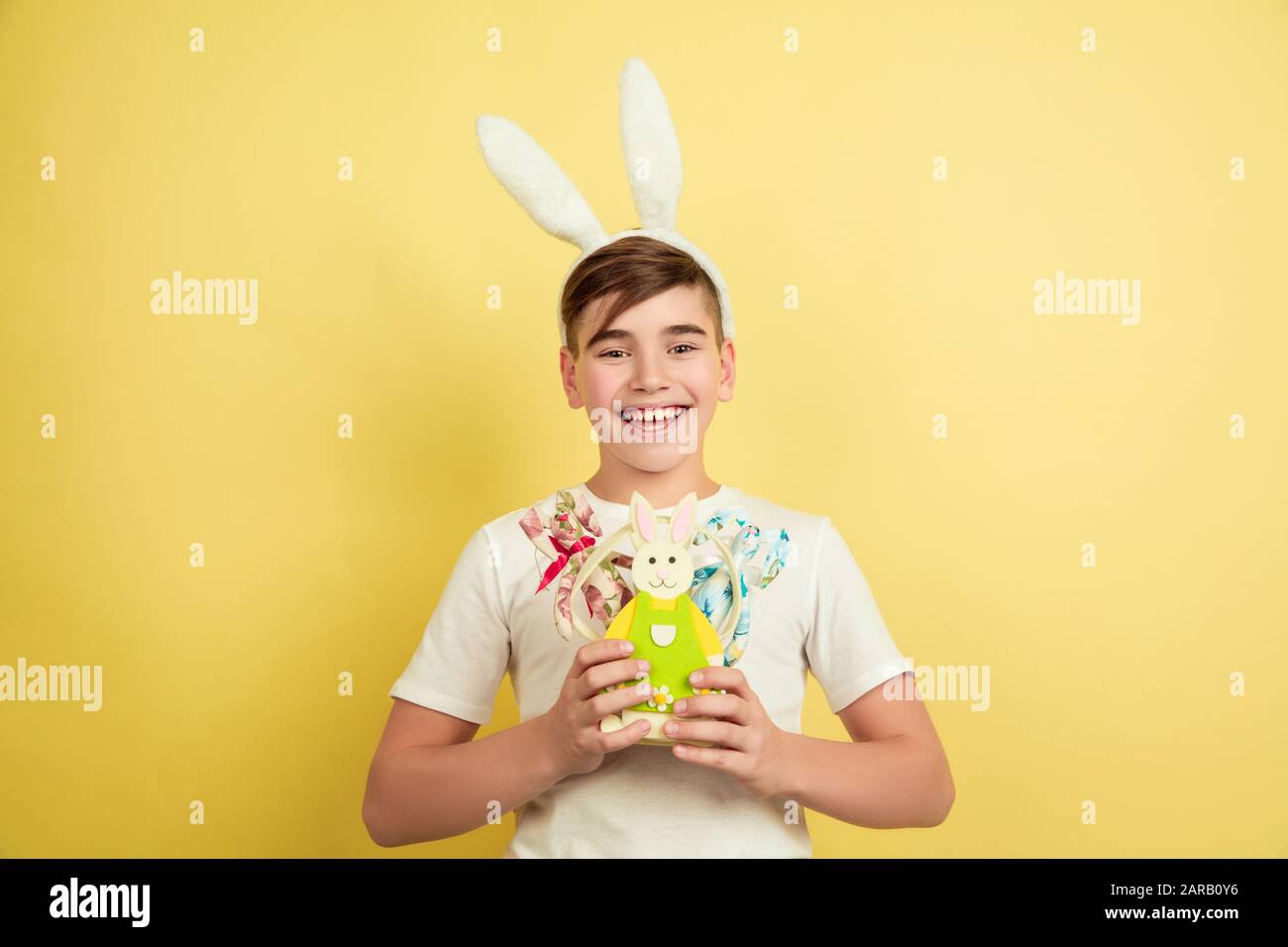 Happy. Decorating. Caucasian boy as an Easter bunny on yellow studio ...