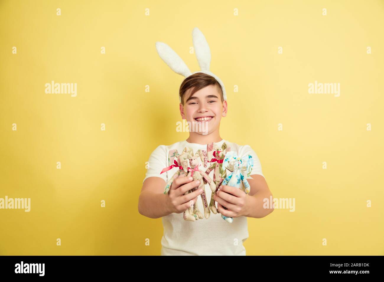 Happy. Decorating. Caucasian boy as an Easter bunny on yellow studio ...