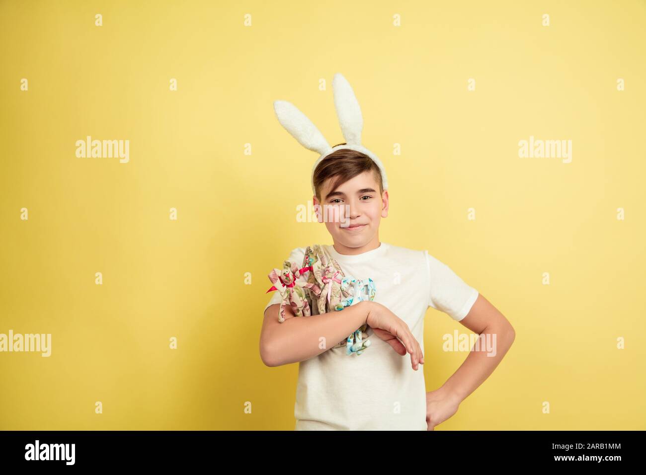 Happy. Decorating. Caucasian boy as an Easter bunny on yellow studio ...