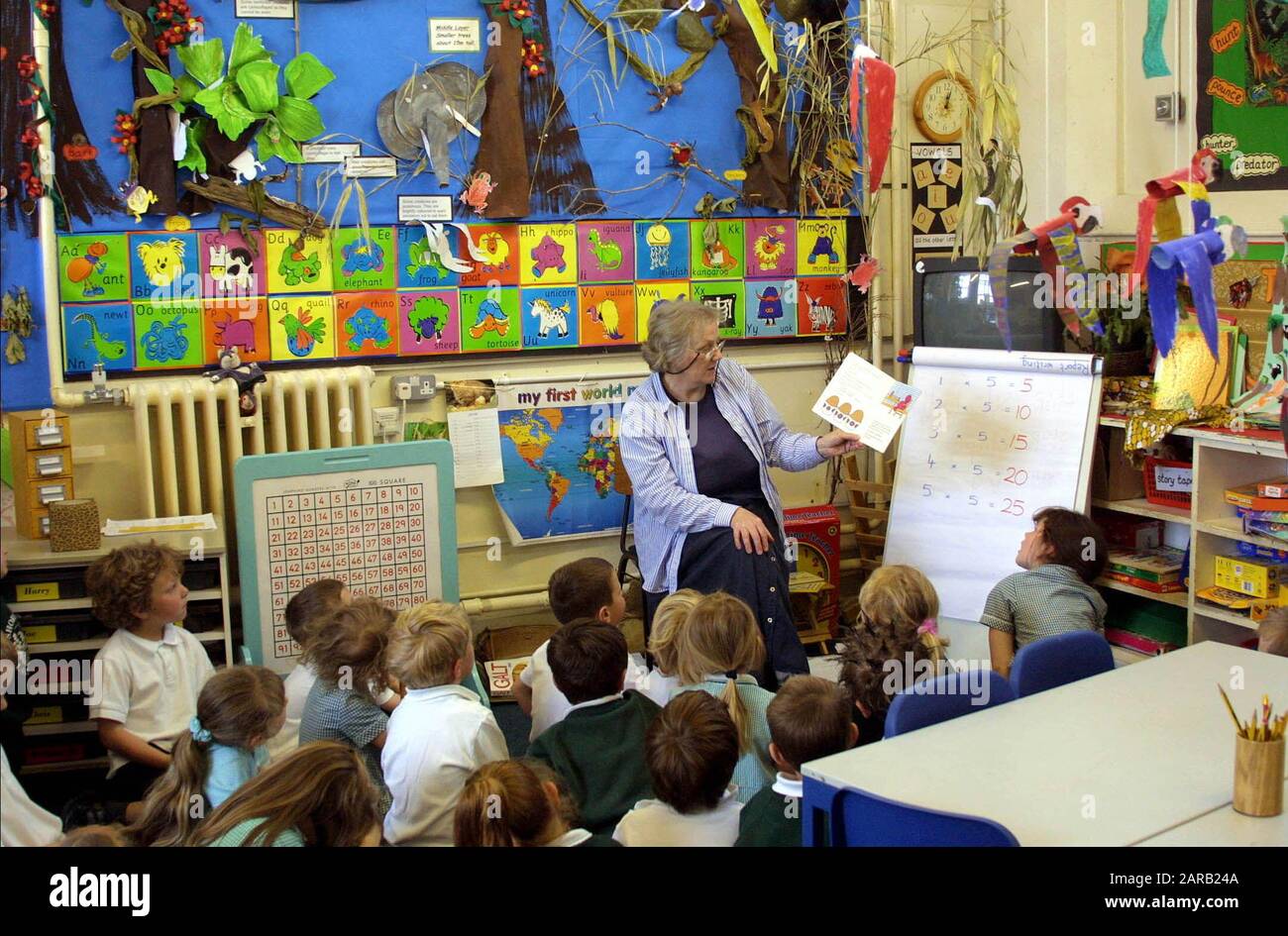 Primary village school classroom with teacher reading a book to young ...