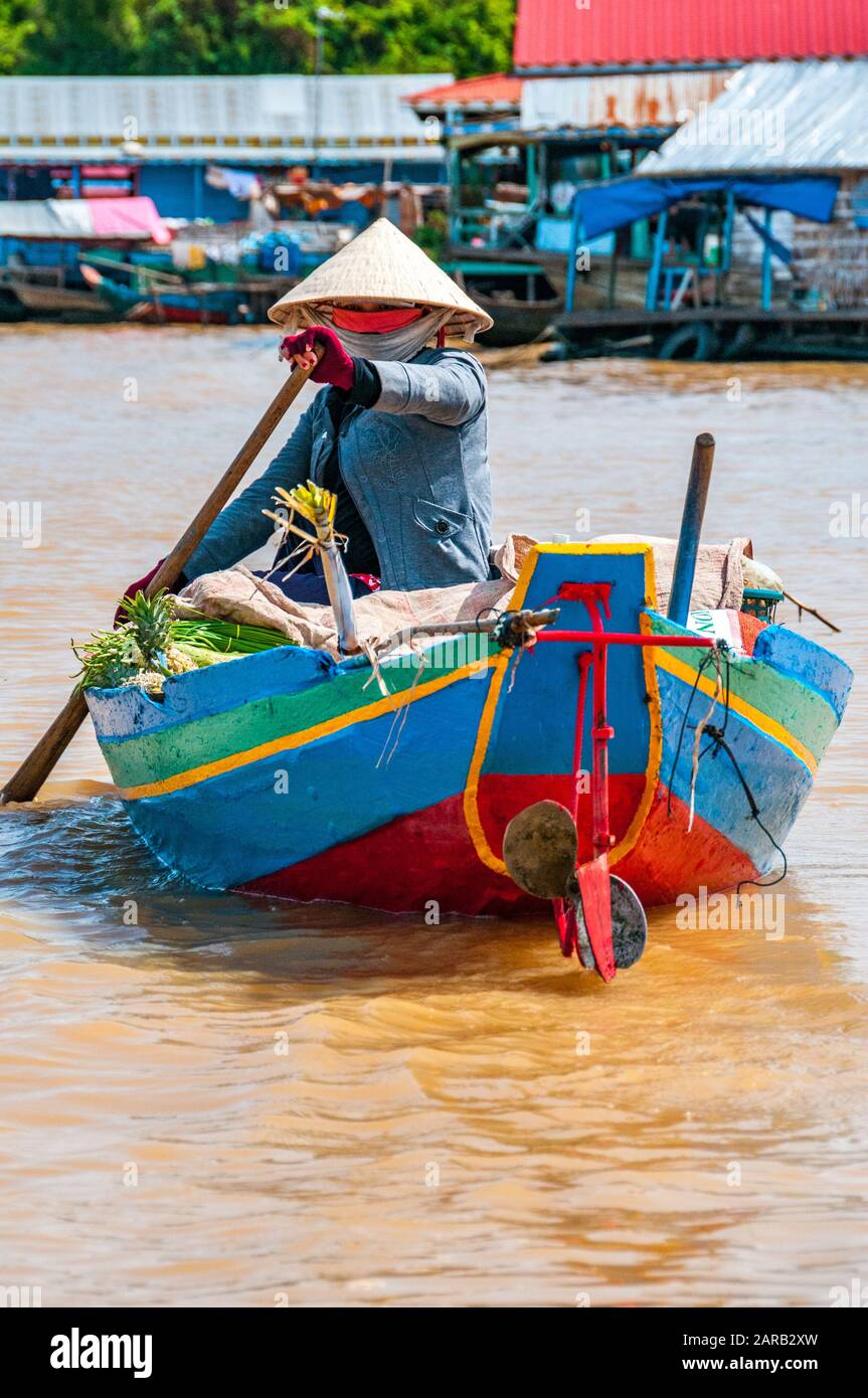 A woman rows a colorful blue, red, green and yellow boat with a ...