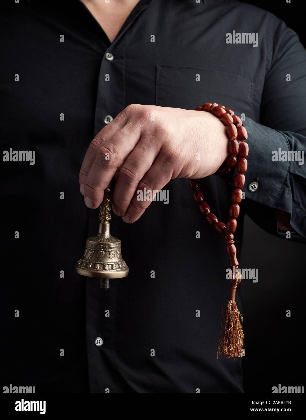 adult man in a black shirt holds a copper Tibetan ritual bell, low key ...