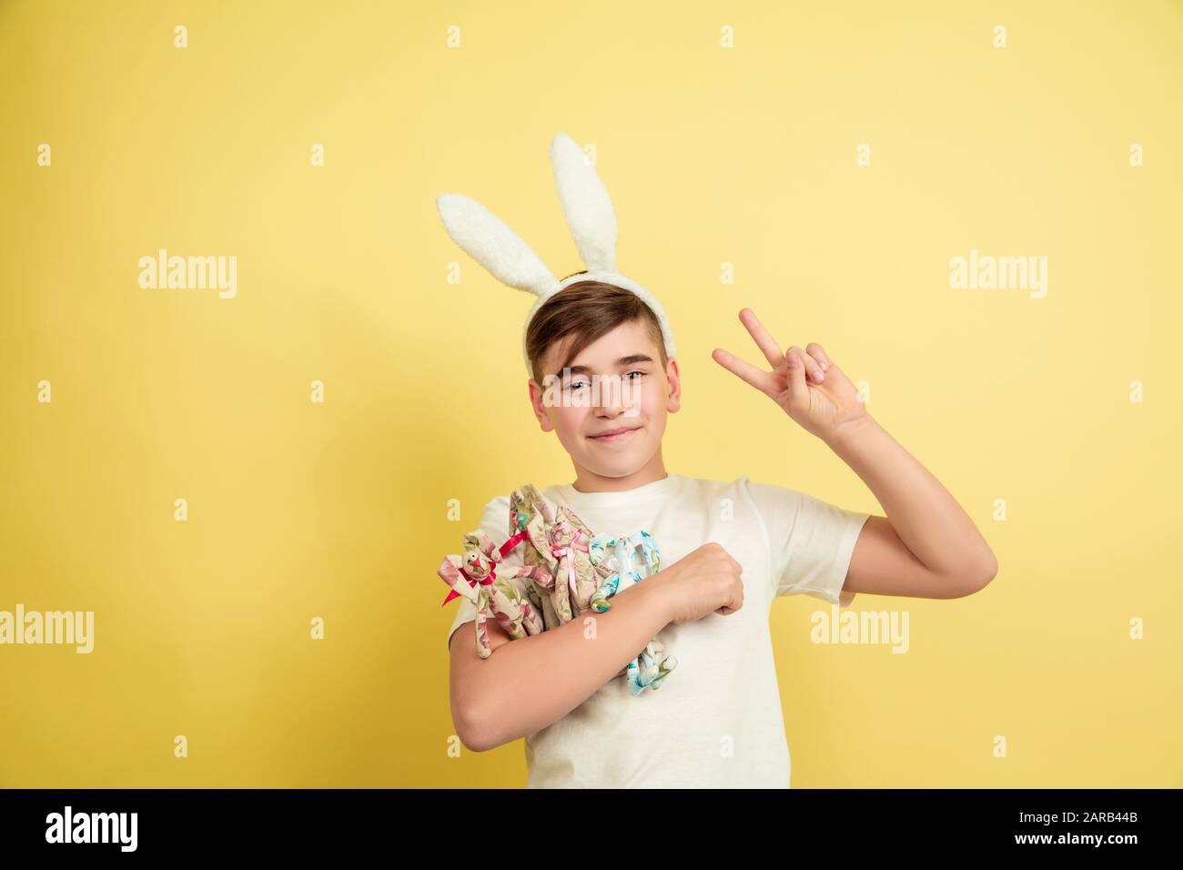 Posing. Decorating. Caucasian boy as an Easter bunny on yellow studio ...