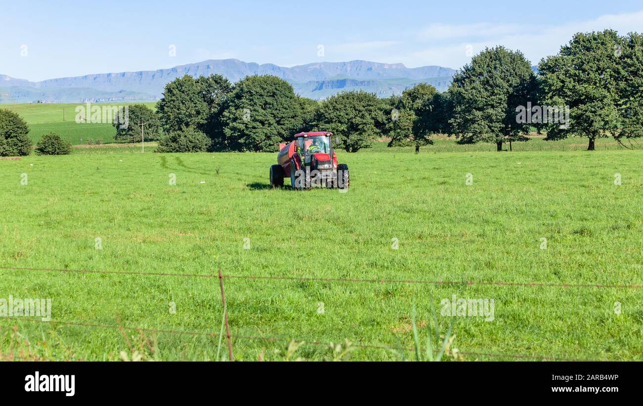 Scenic summer mountain farmlands with red tractor with trailer in green ...