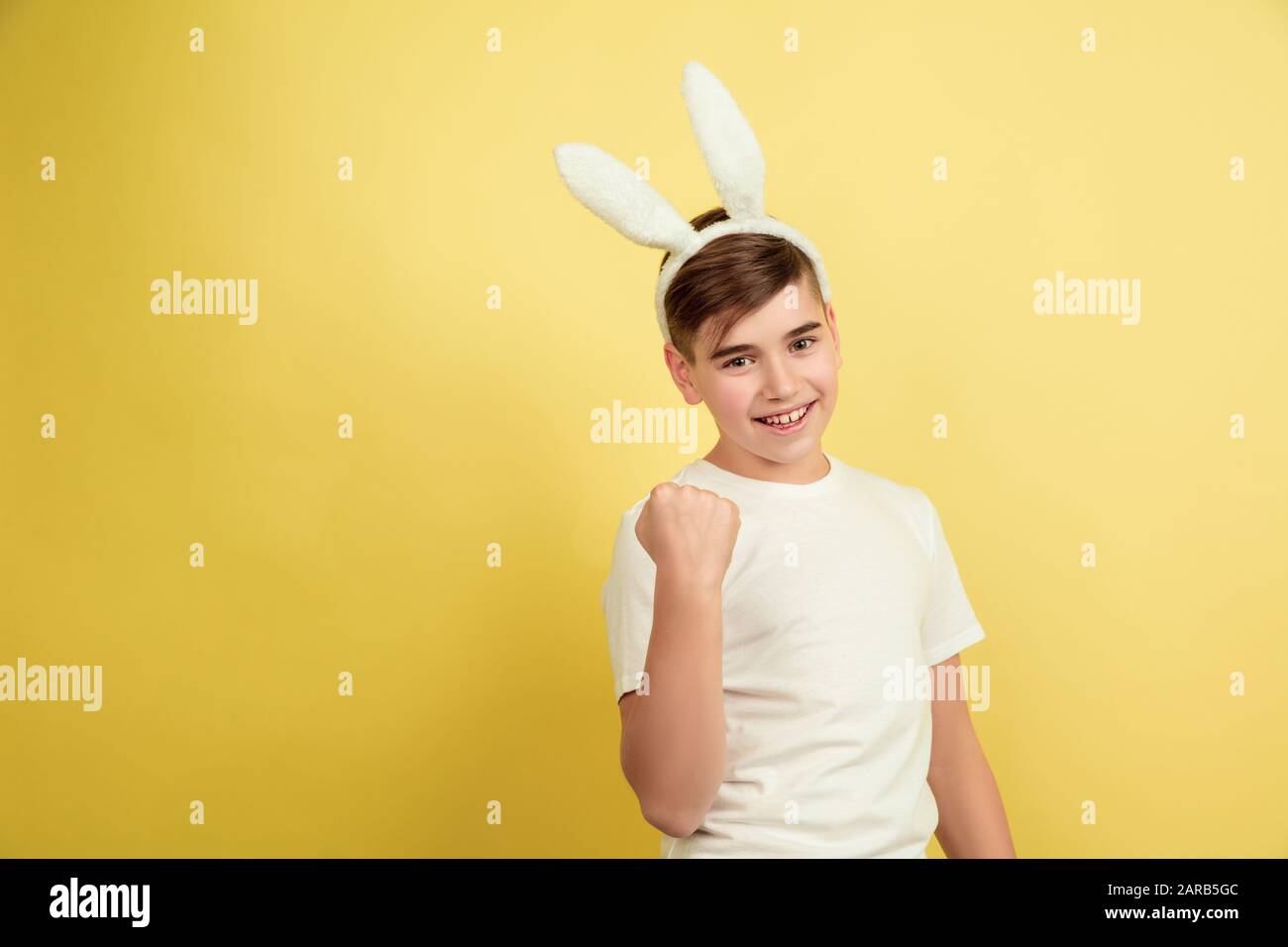 Celebrating win. Caucasian boy as an Easter bunny on yellow studio ...