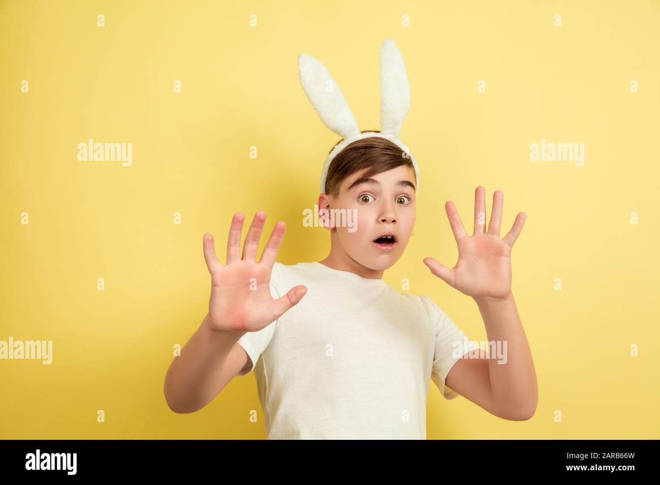 Scared, shocked. Caucasian boy as an Easter bunny on yellow studio ...