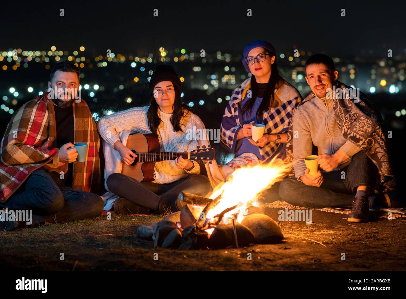 Group of people having fun sitting near bonfire outdoors at night ...