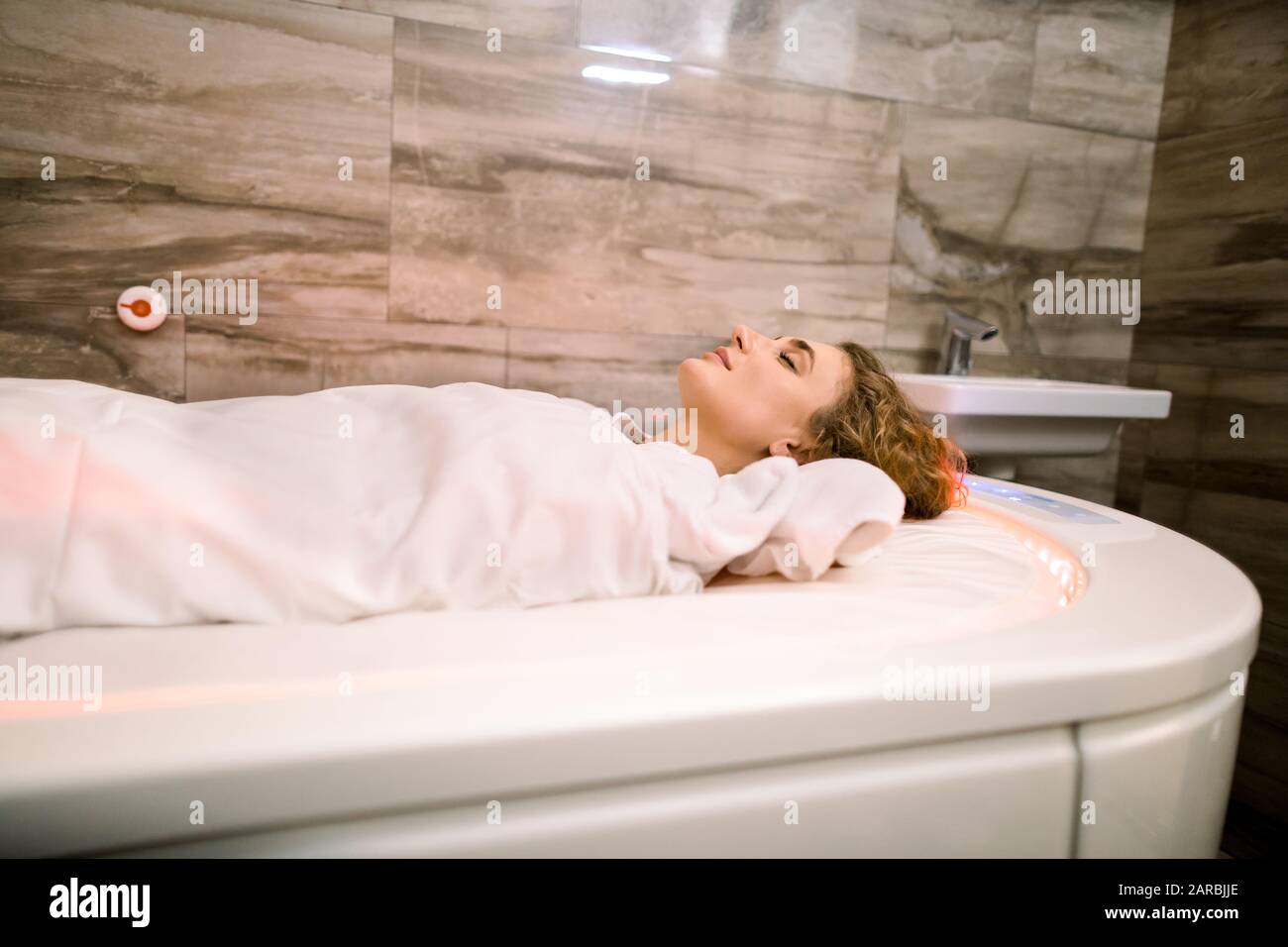 Close up portrait of young beautiful woman lying on special hot spa bed ...