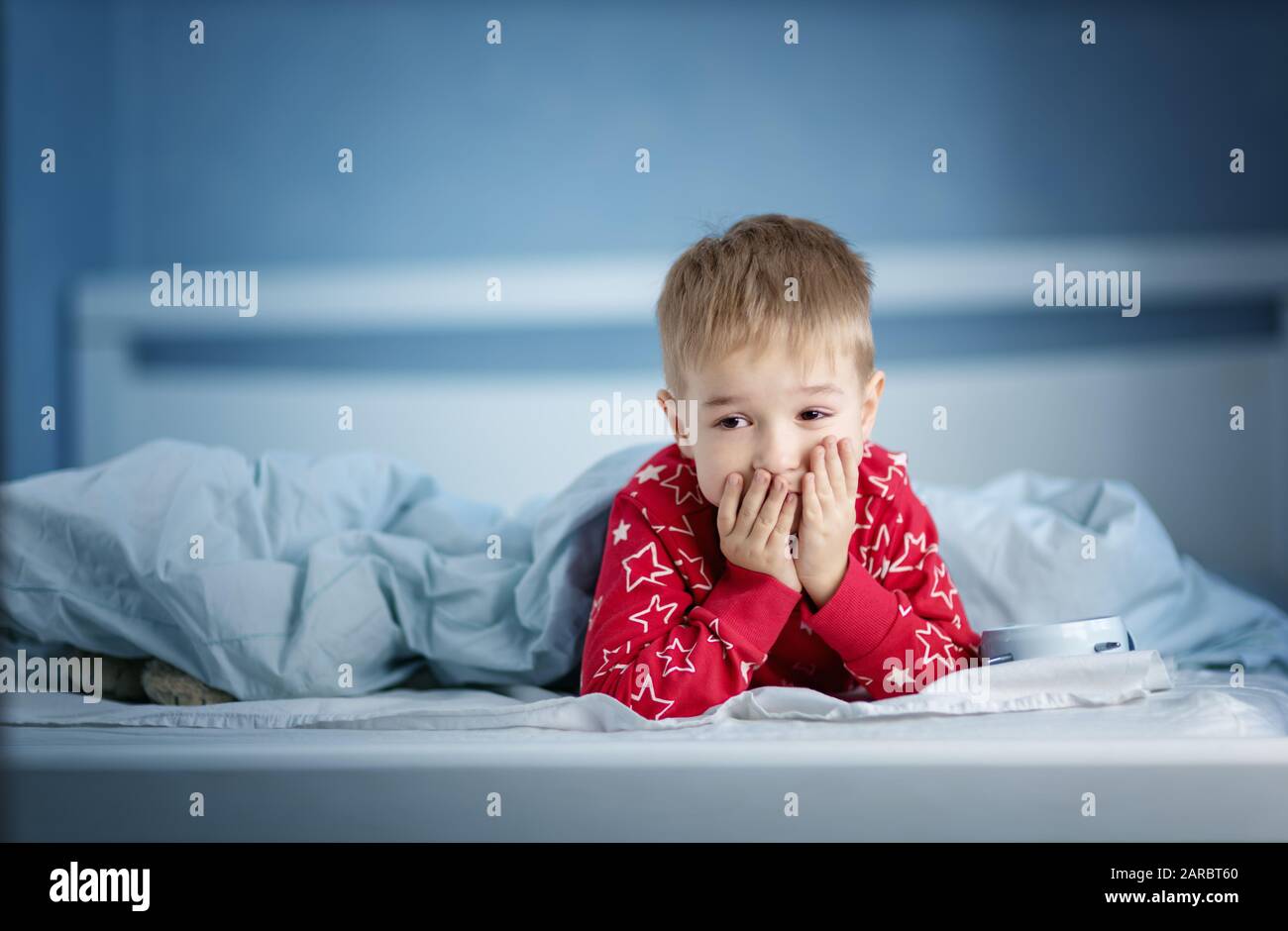 Sleepy boy lying in bed with blue beddings Stock Photo - Alamy
