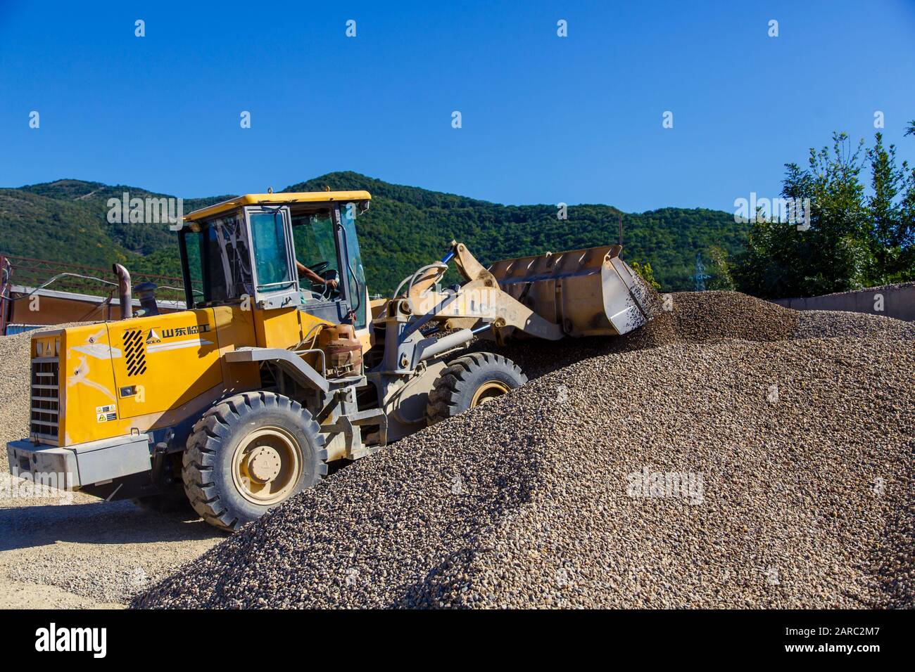 Tractor-loader loads rubble on a bright Sunny day. Piles of rubble. A ...