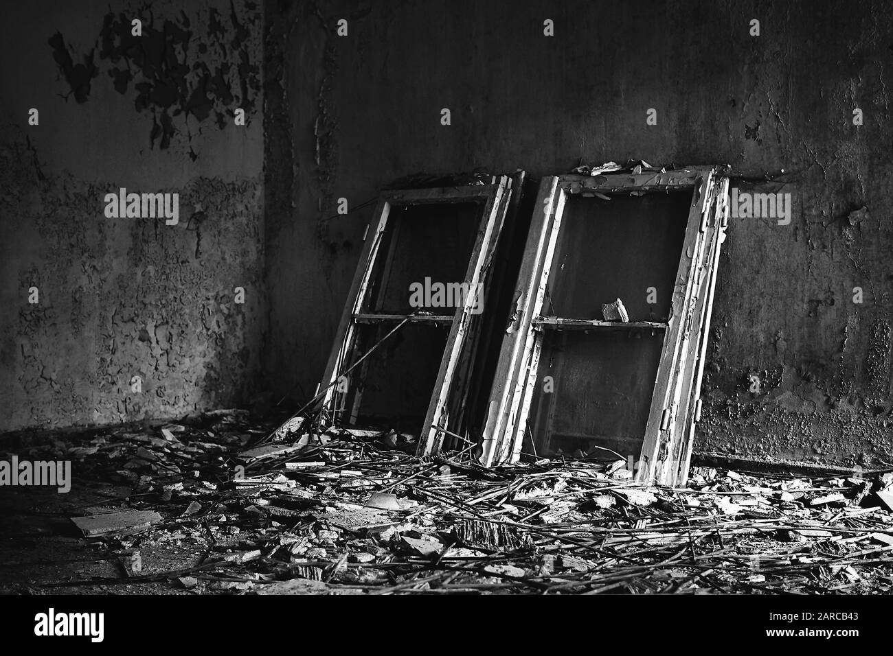 Grayscale shot of window frames placed on a messy floor in an old house ...
