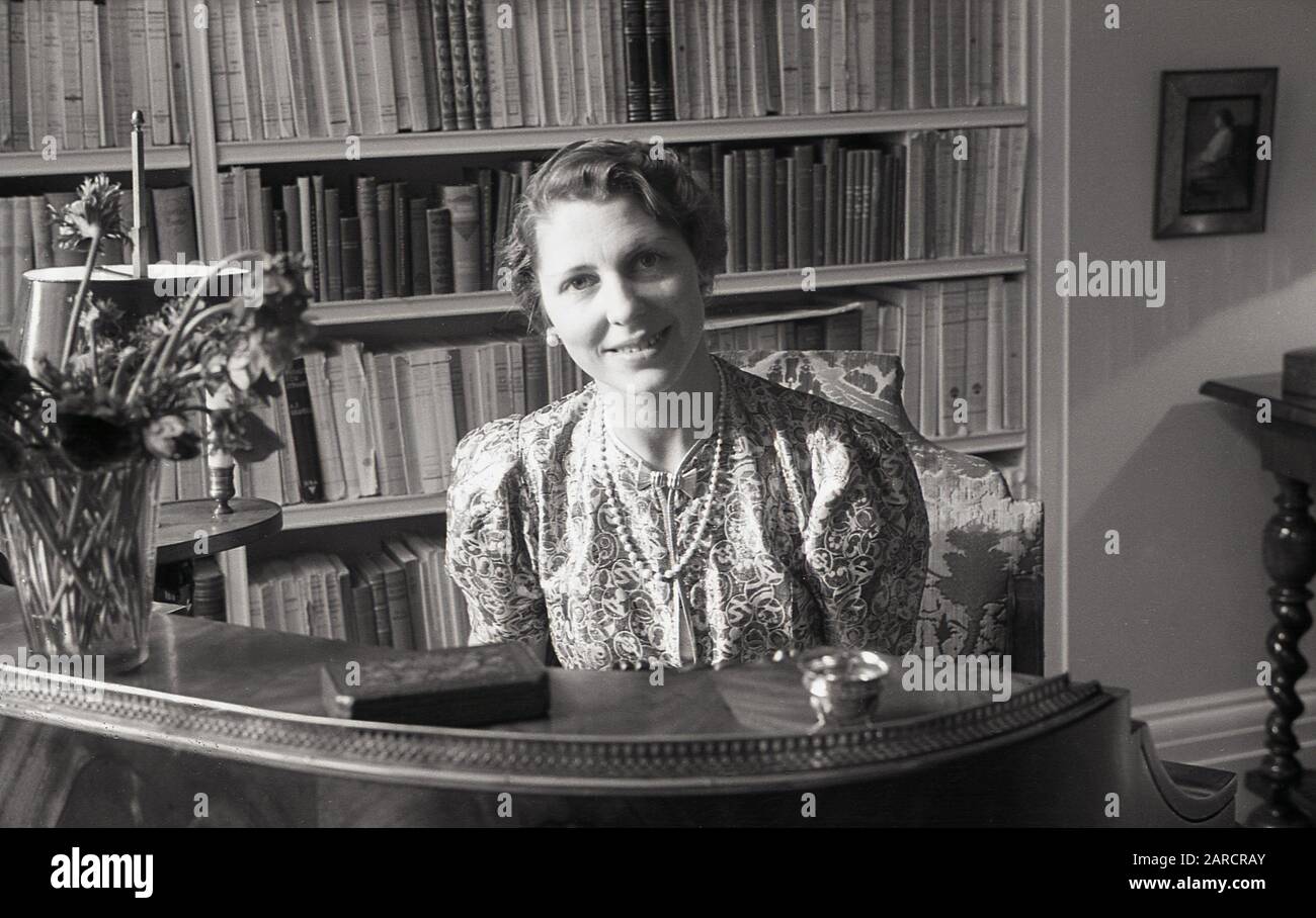1950s, historical, an elegant lady in her book lined study sitting at ...