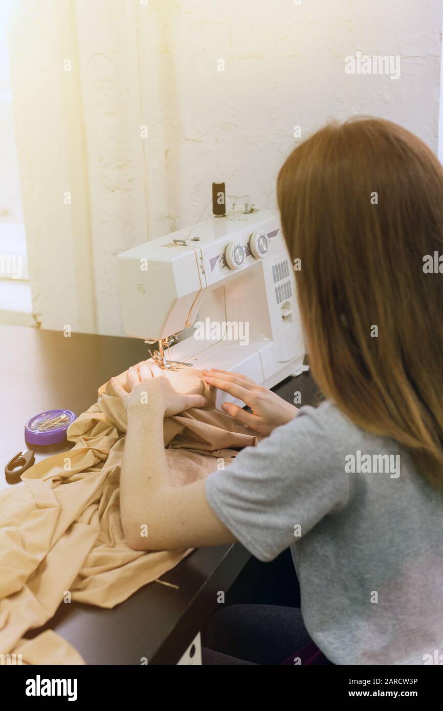 A young woman sews on a sewing machine in the Studio. Cute seamstress ...