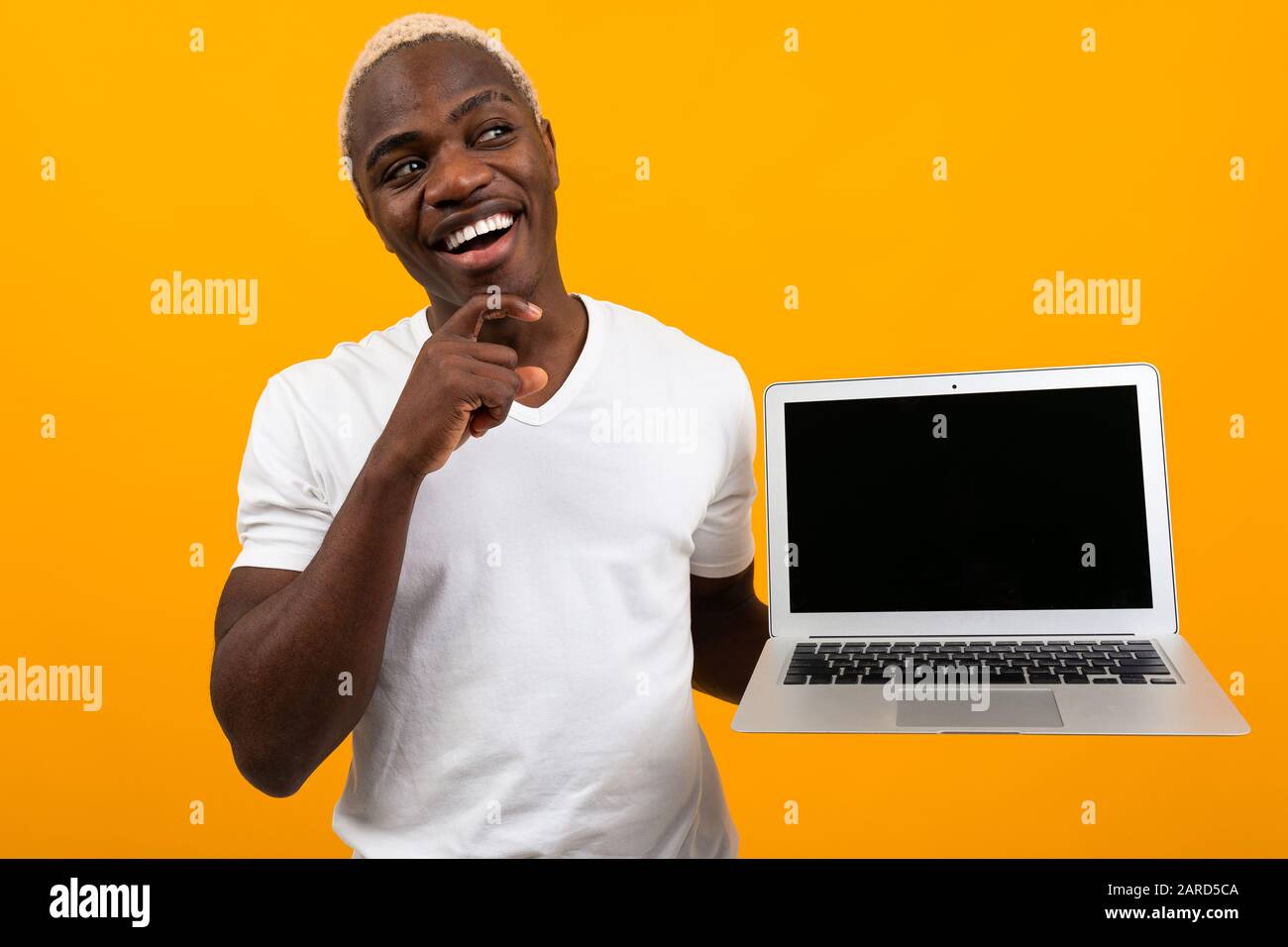 joyful smiling african man holding laptop with mockup on yellow ...