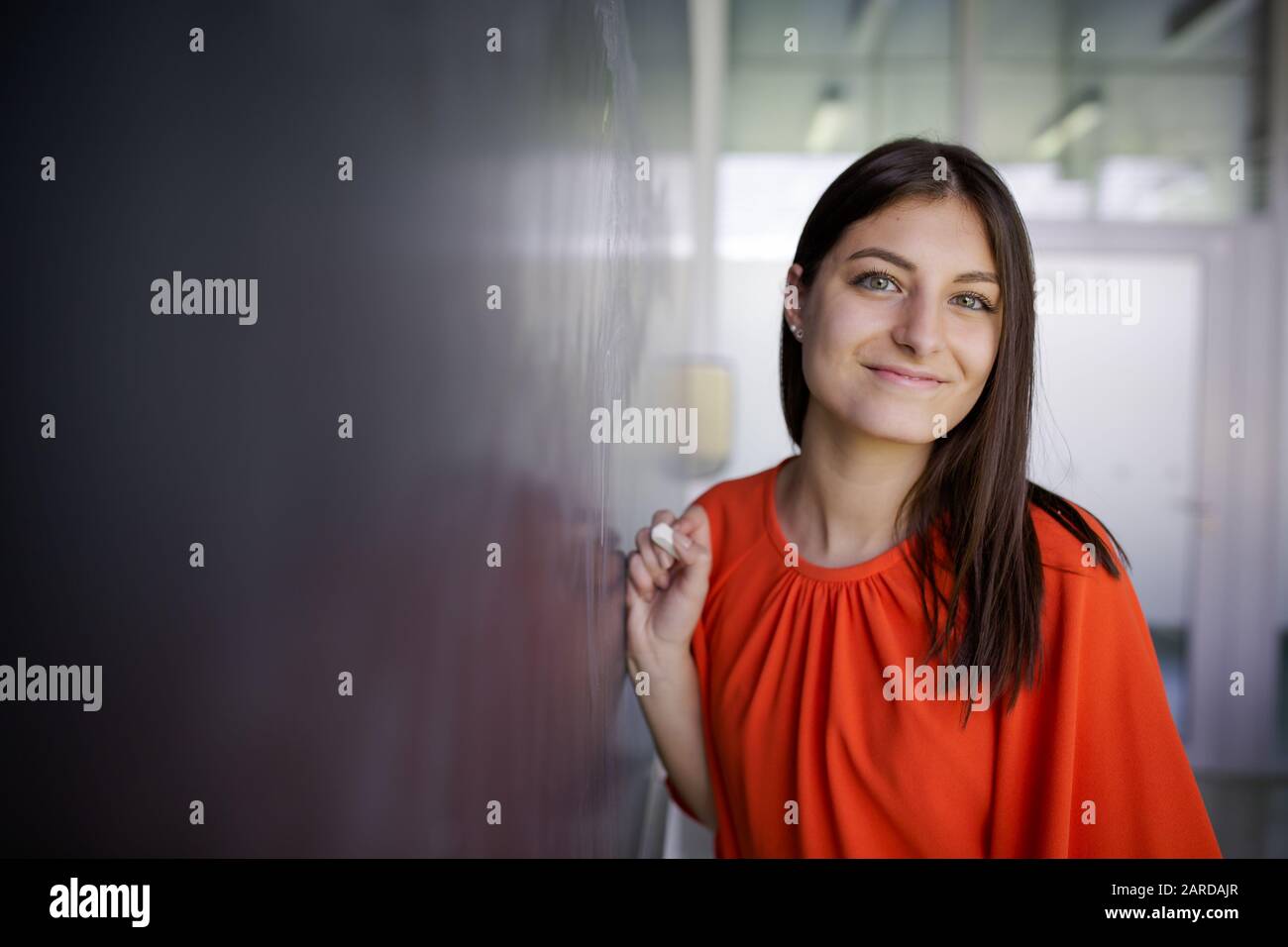 Pretty, young college student/young teacher writing on the chalkboard ...