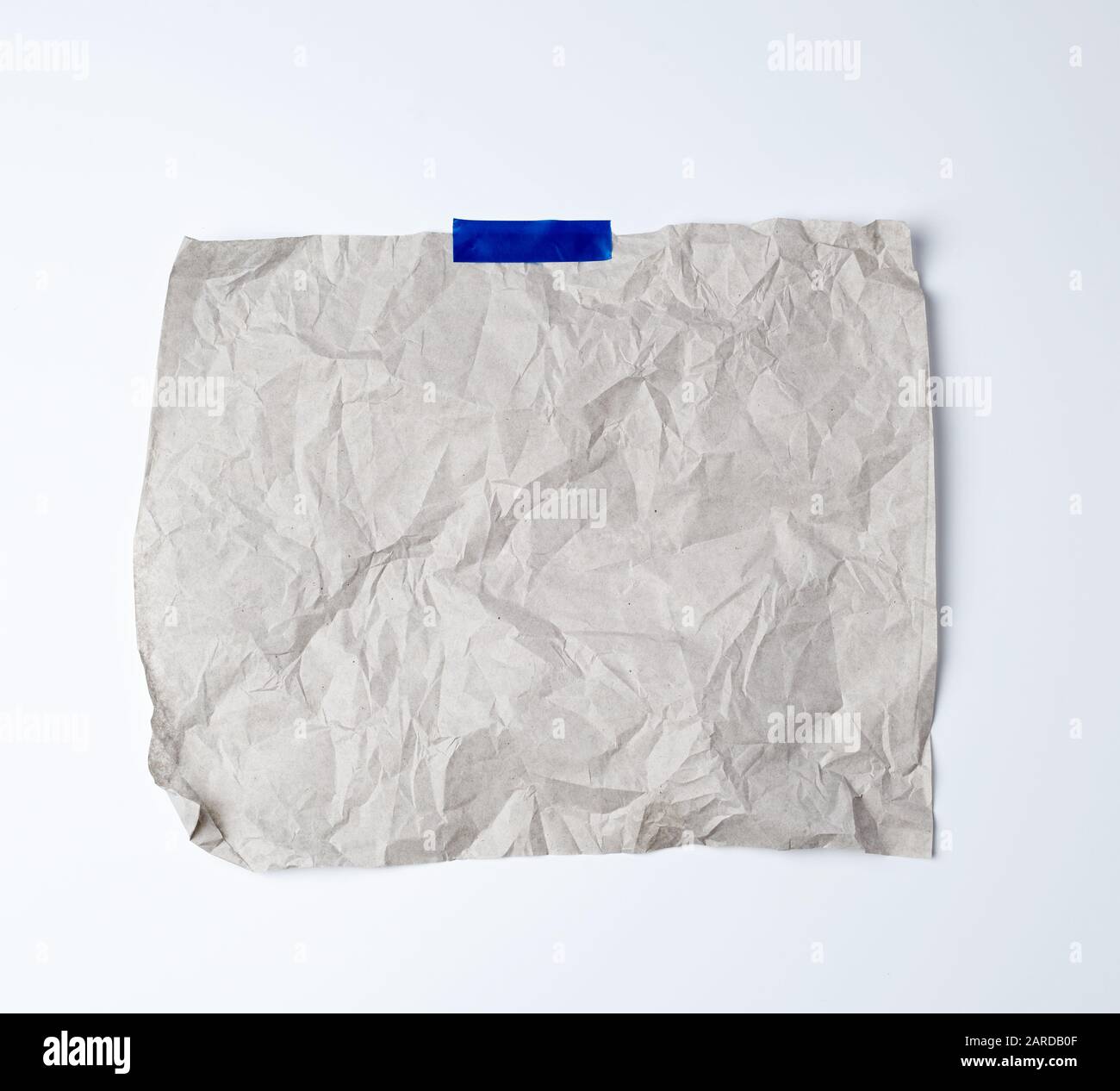 gray crumpled sheet of paper glued with blue adhesive tape on a white ...