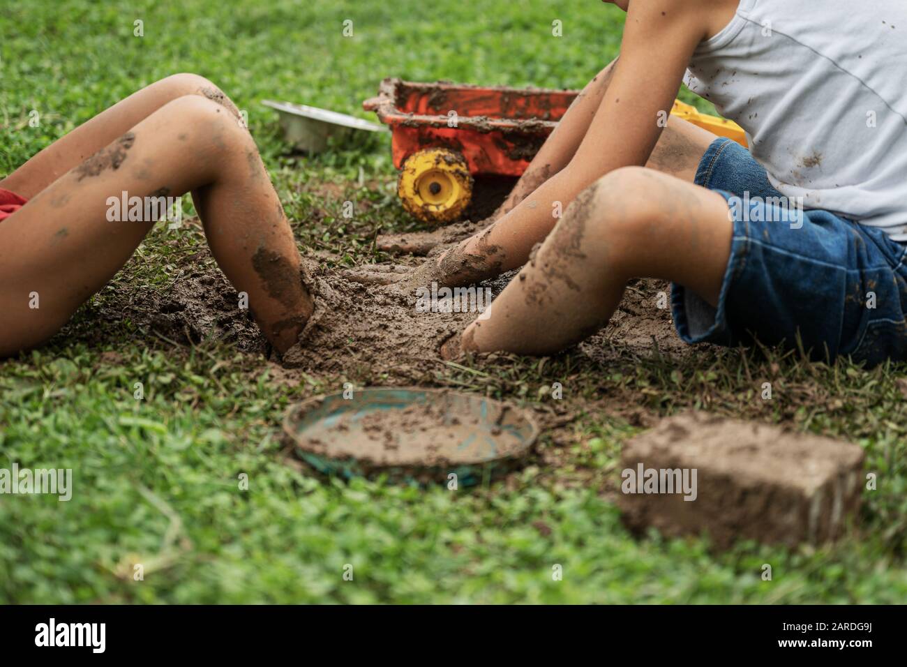 Two boys playing with mud in backyard digging their foot in the dirt ...