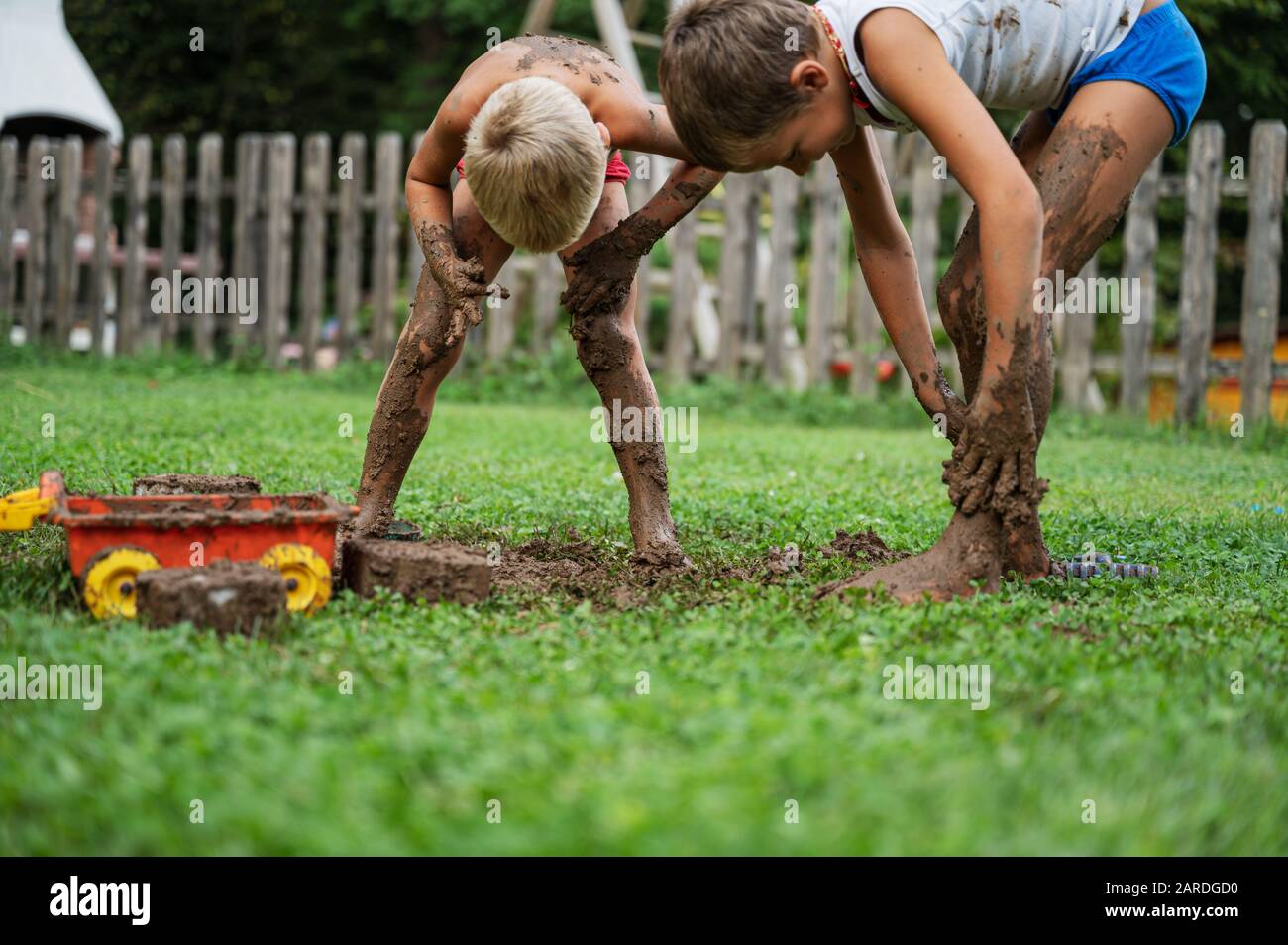 Two brothers playing with mud outside in backyard spreading it all over ...