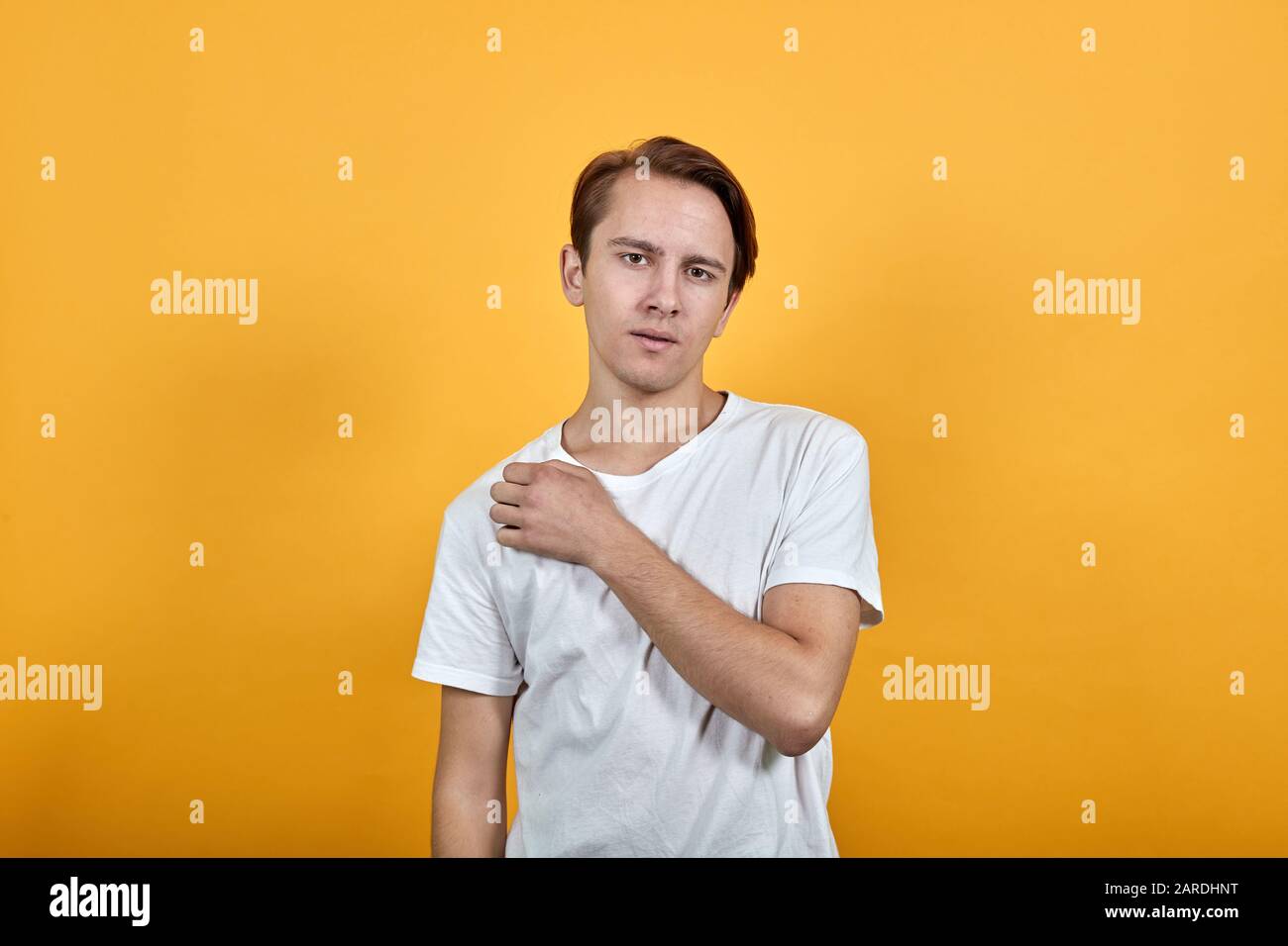 indifferent man in white t-shirt on yellow background looks forward ...