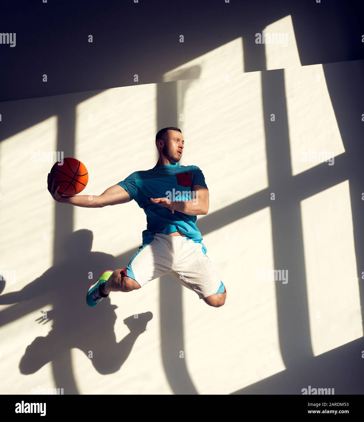 Young athletic basketball player jumping with ball in front of wall ...