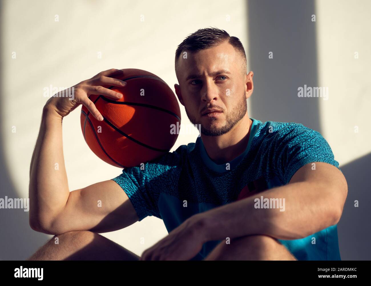 Portrait of basketball player holding ball on shoulder and sitting near ...