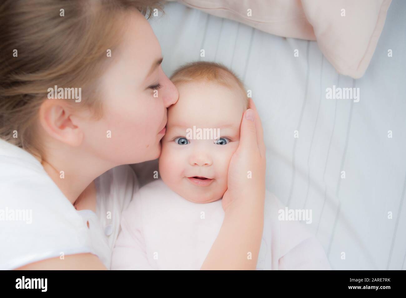 Happy mother kisses baby lying on the bed. Top view Stock Photo - Alamy