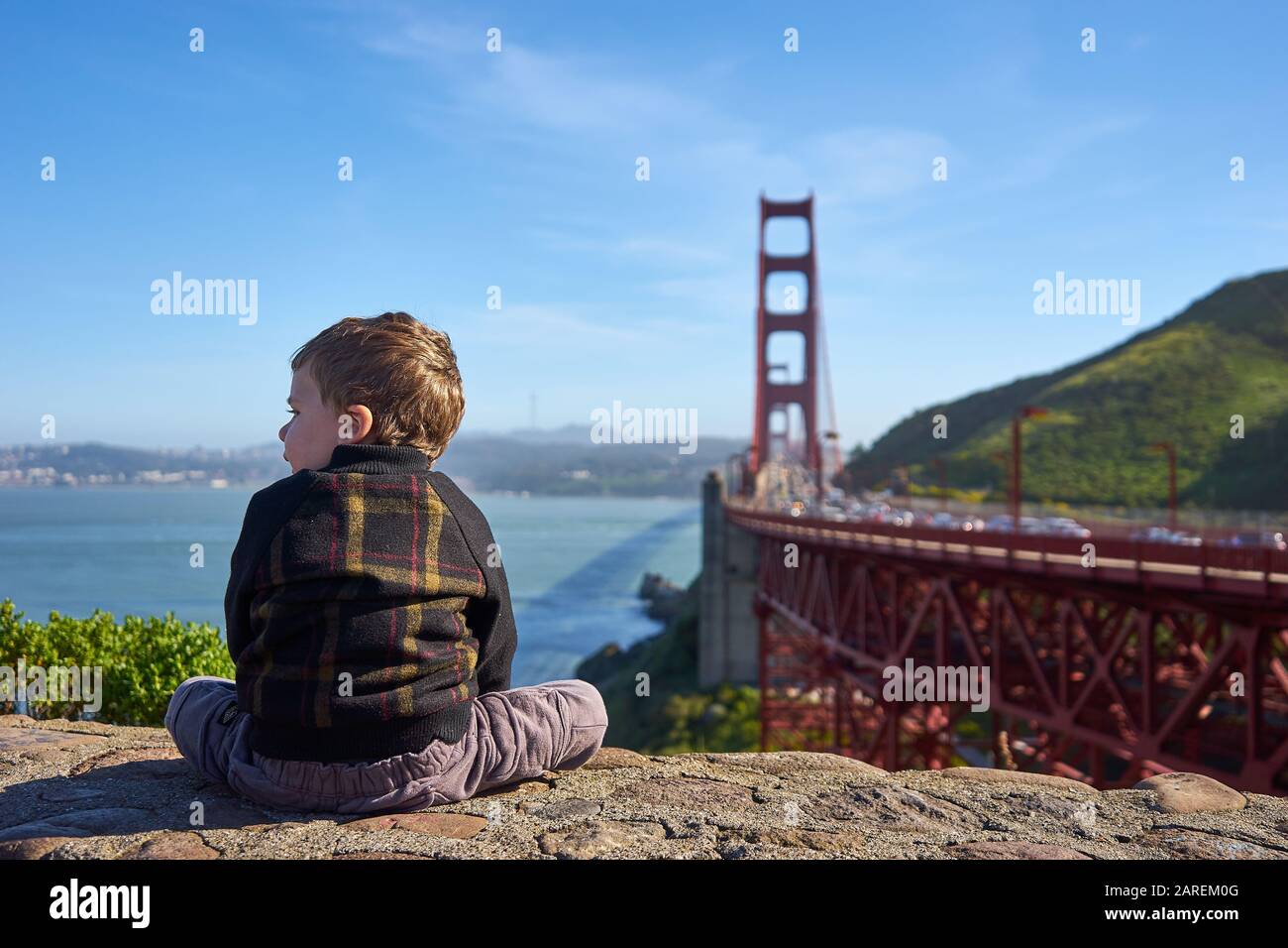A young boy sitting on a stone retaining wall at a lookout by the ...