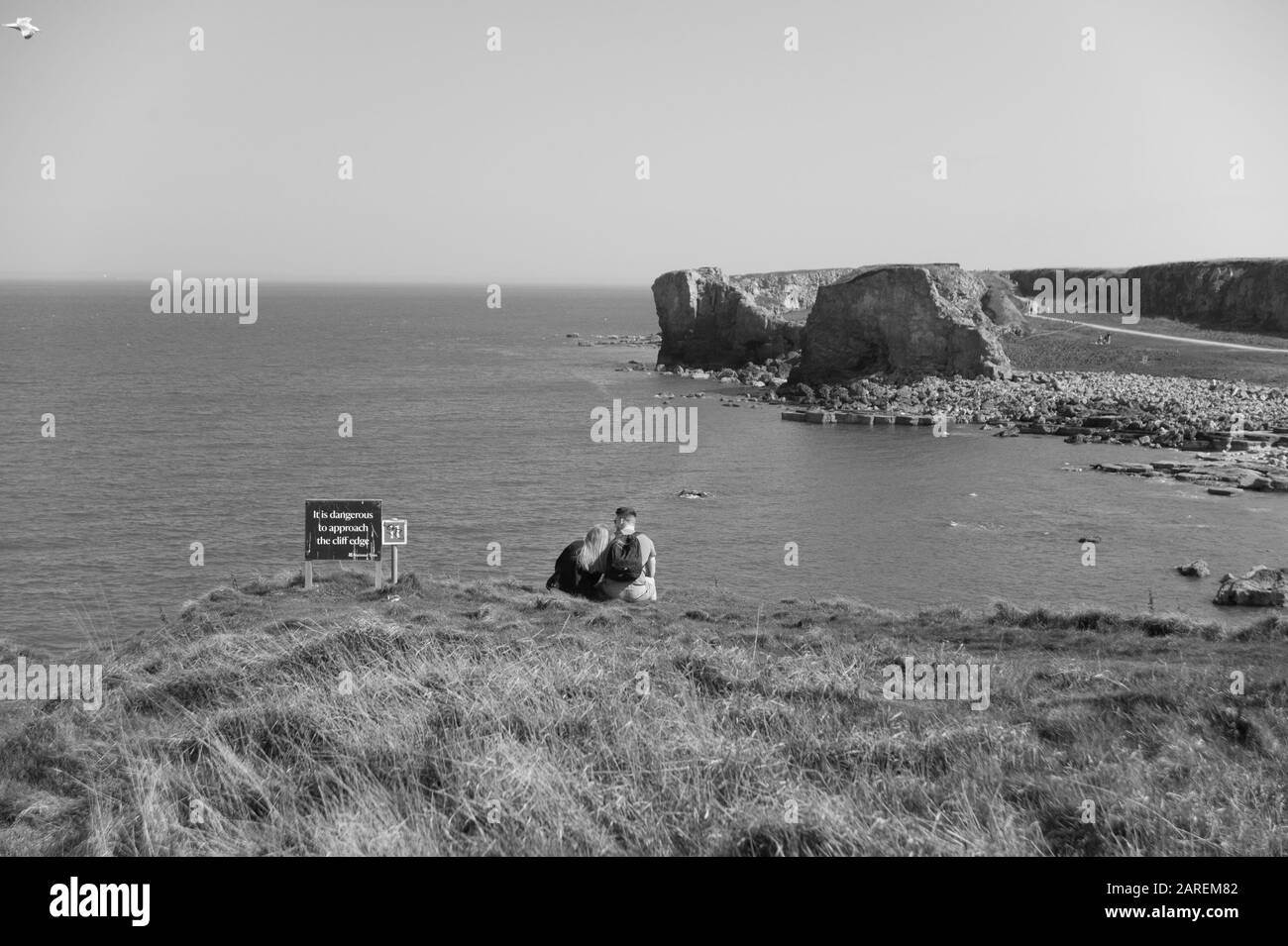 Couple sitting by cliff and danger sign,South Shields Stock Photo - Alamy