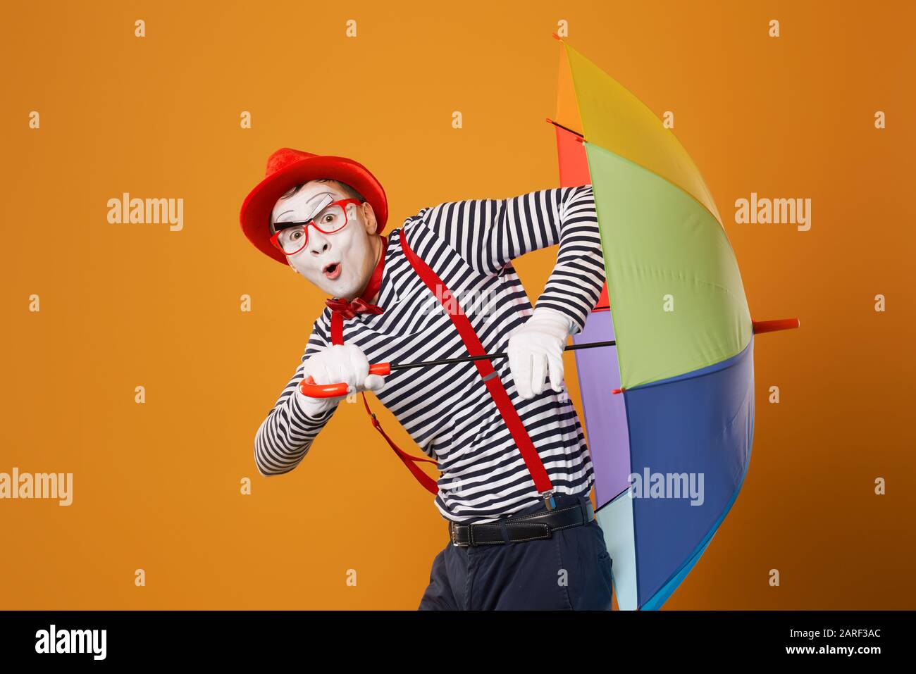Mime man with multi-colored umbrella on empty orange background in ...