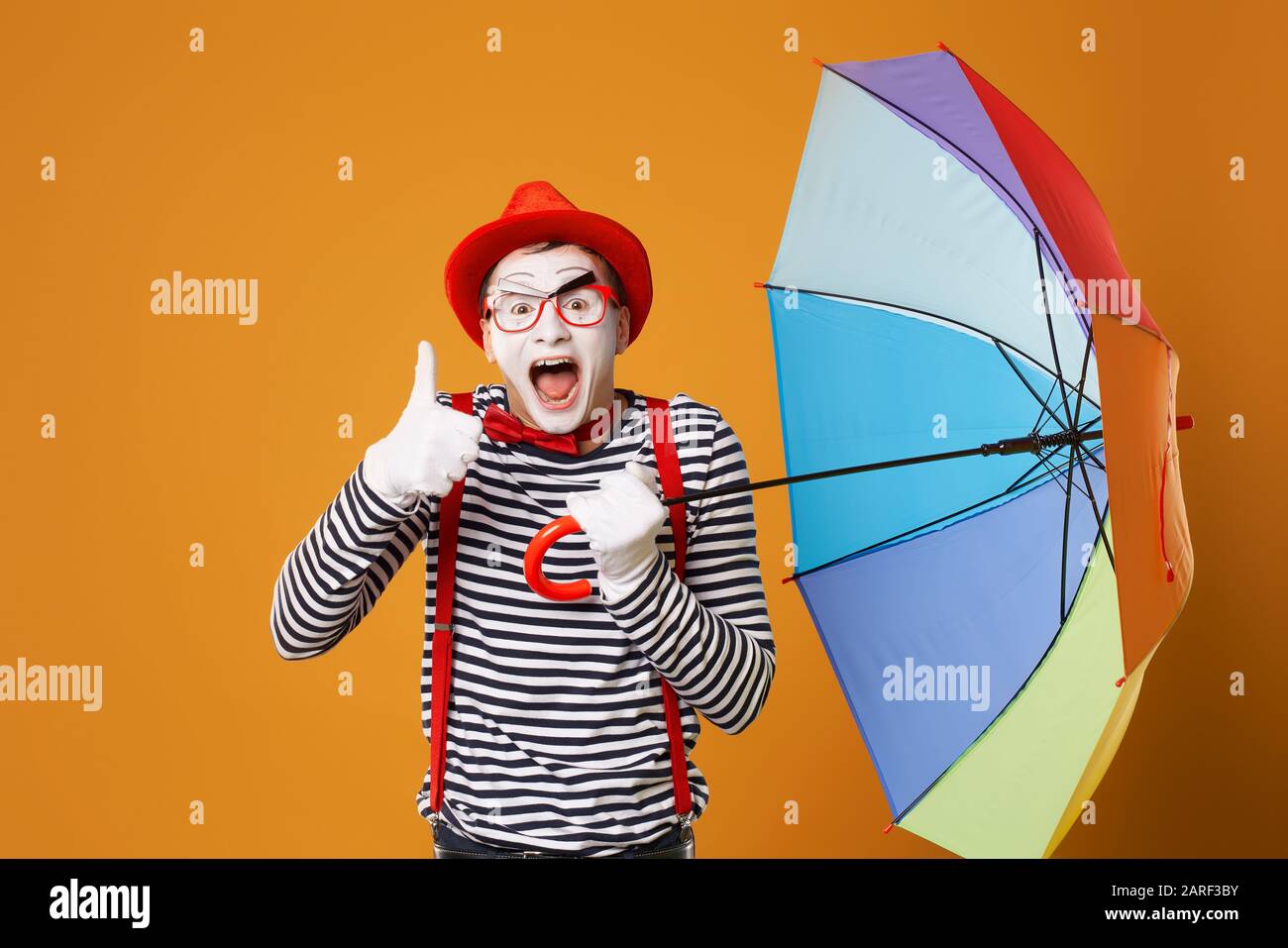 Cheerful mime with multi-colored umbrella isolated on blank orange ...