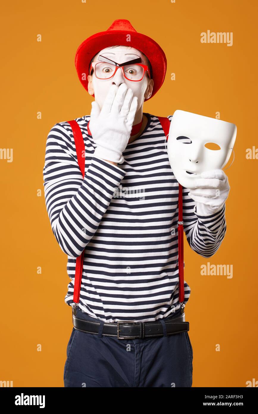 Surprised mime in red hat and in vest with white mask on blank orange ...