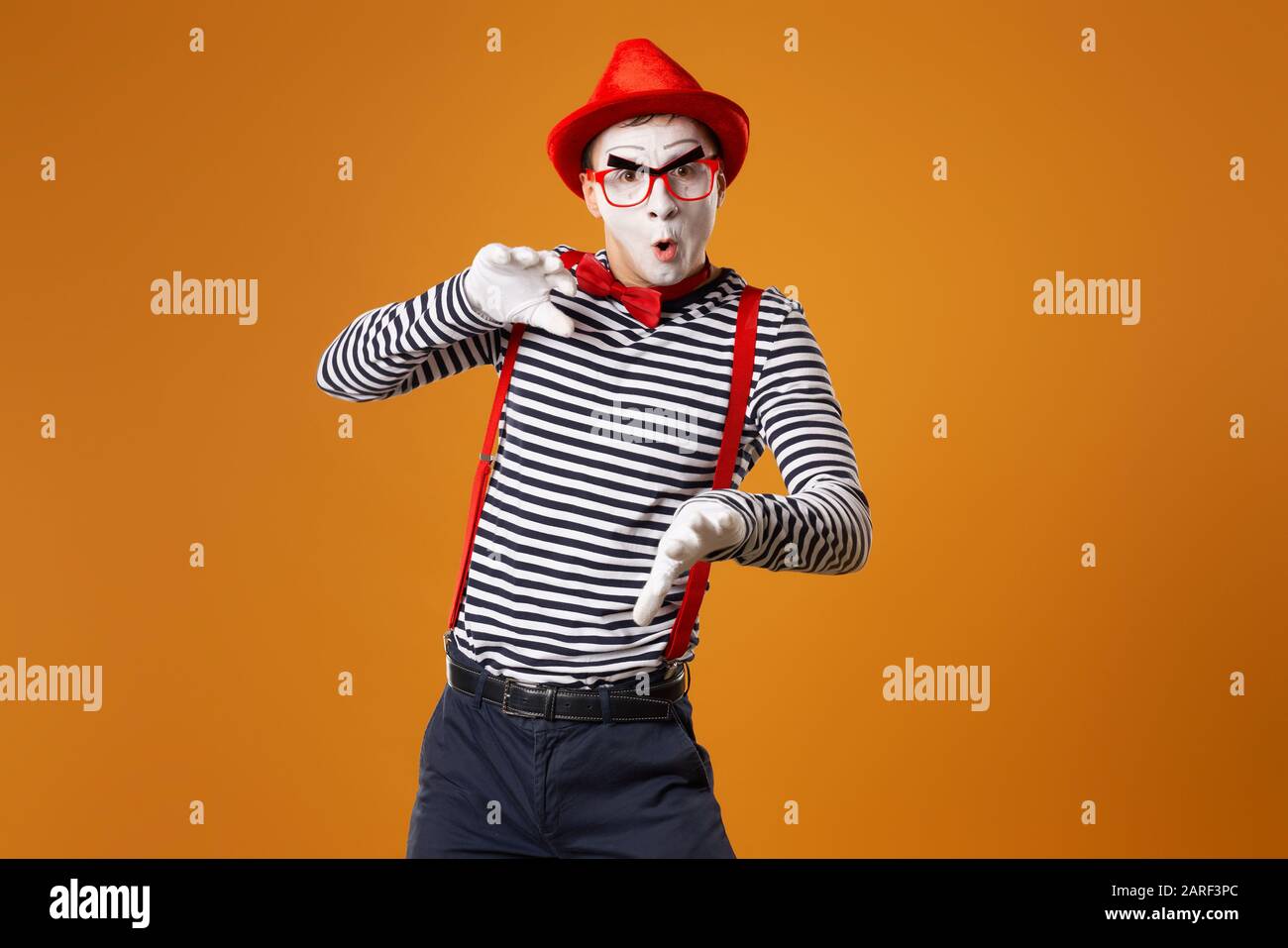 Mime man in white gloves and red hat looking at camera on empty orange ...